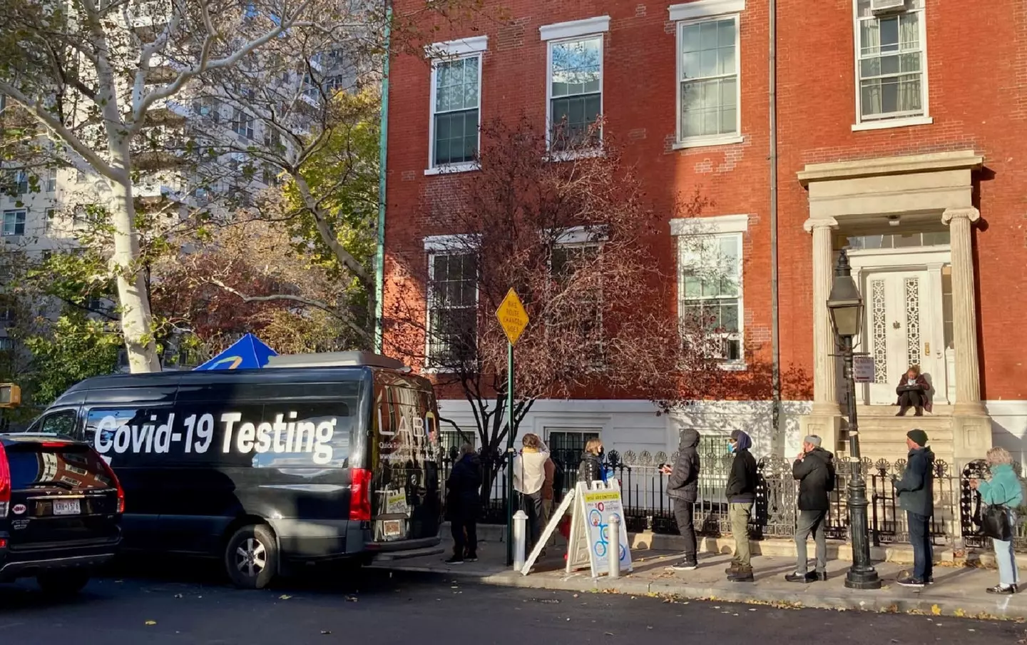 Människor i masker väntar på en gata i New York City på dagtid för gratis COVID-19-testning vid en blå lastbil