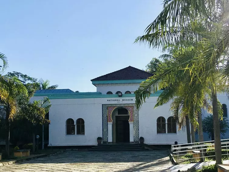 Bangunan museum berwarna putih dan hijau yang dikelilingi oleh pohon palem