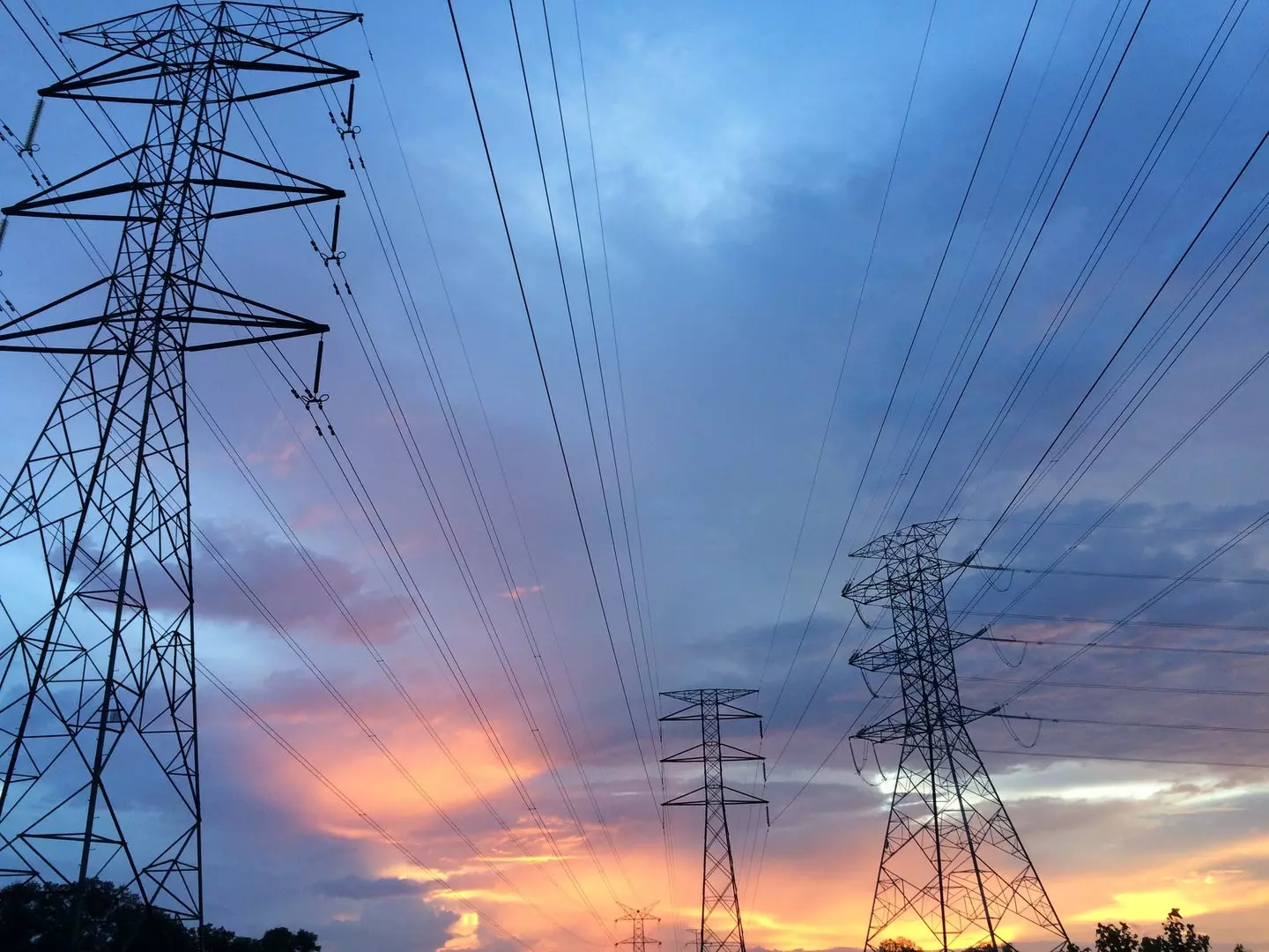 Buludlu gün batımı səmasına qarşı elektrik xətləri.