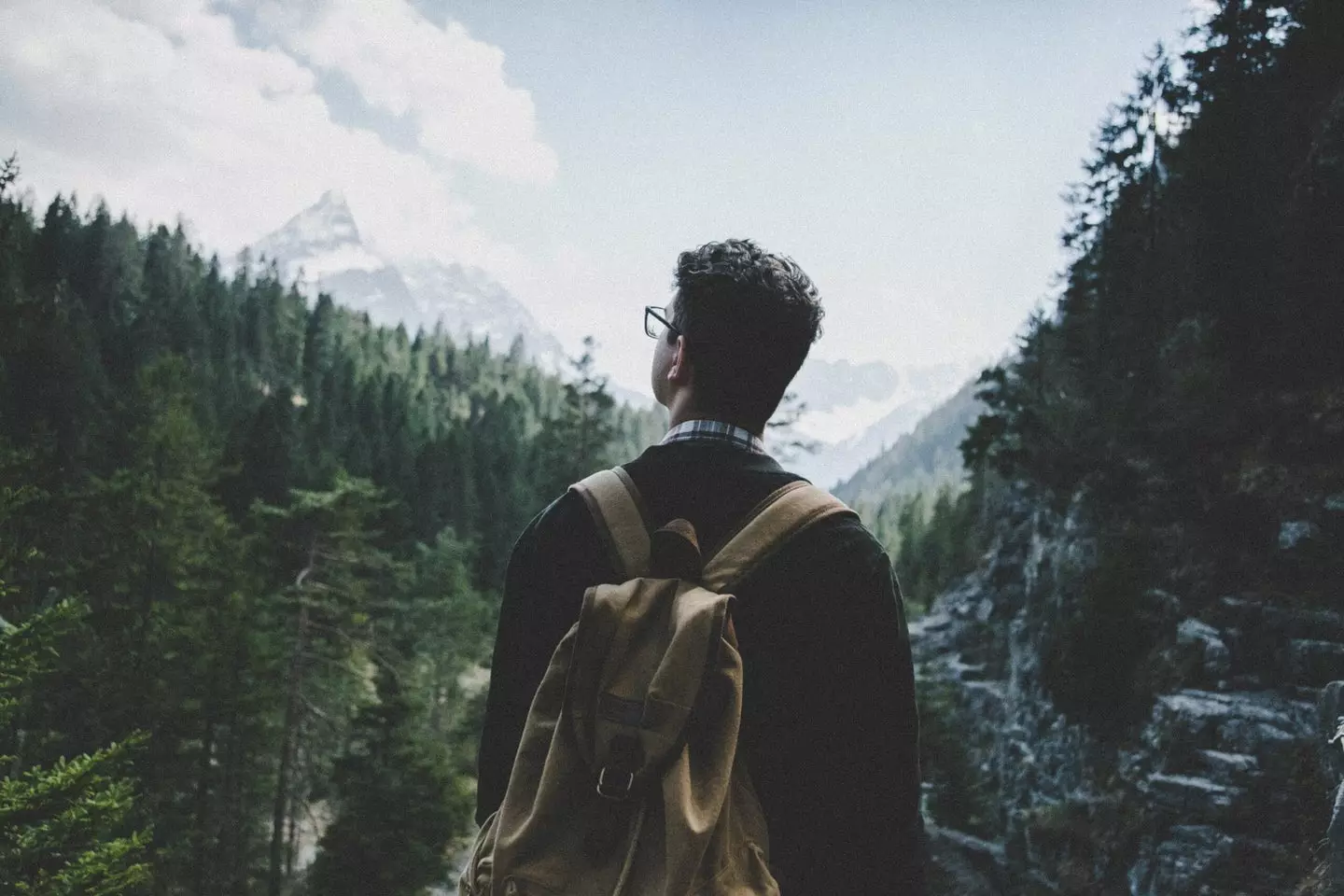 Man dy't op Rocky Mountain stiet ûnder wite bewolkte loft om geastlike sûnens yn 'e natuer te ferbetterjen